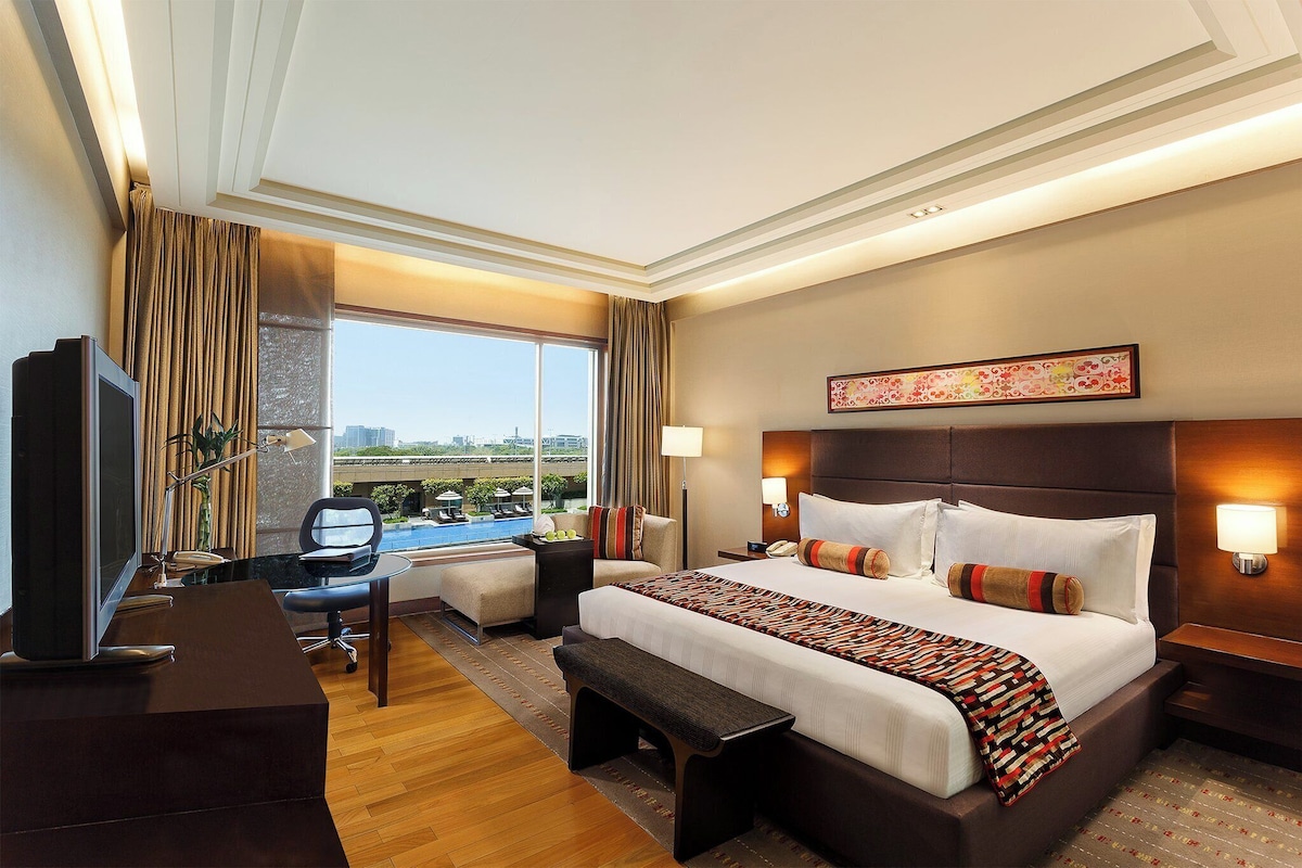 Quarto de hotel com cama grande, escrivaninha, cadeira, televisão e vista para a cidade.