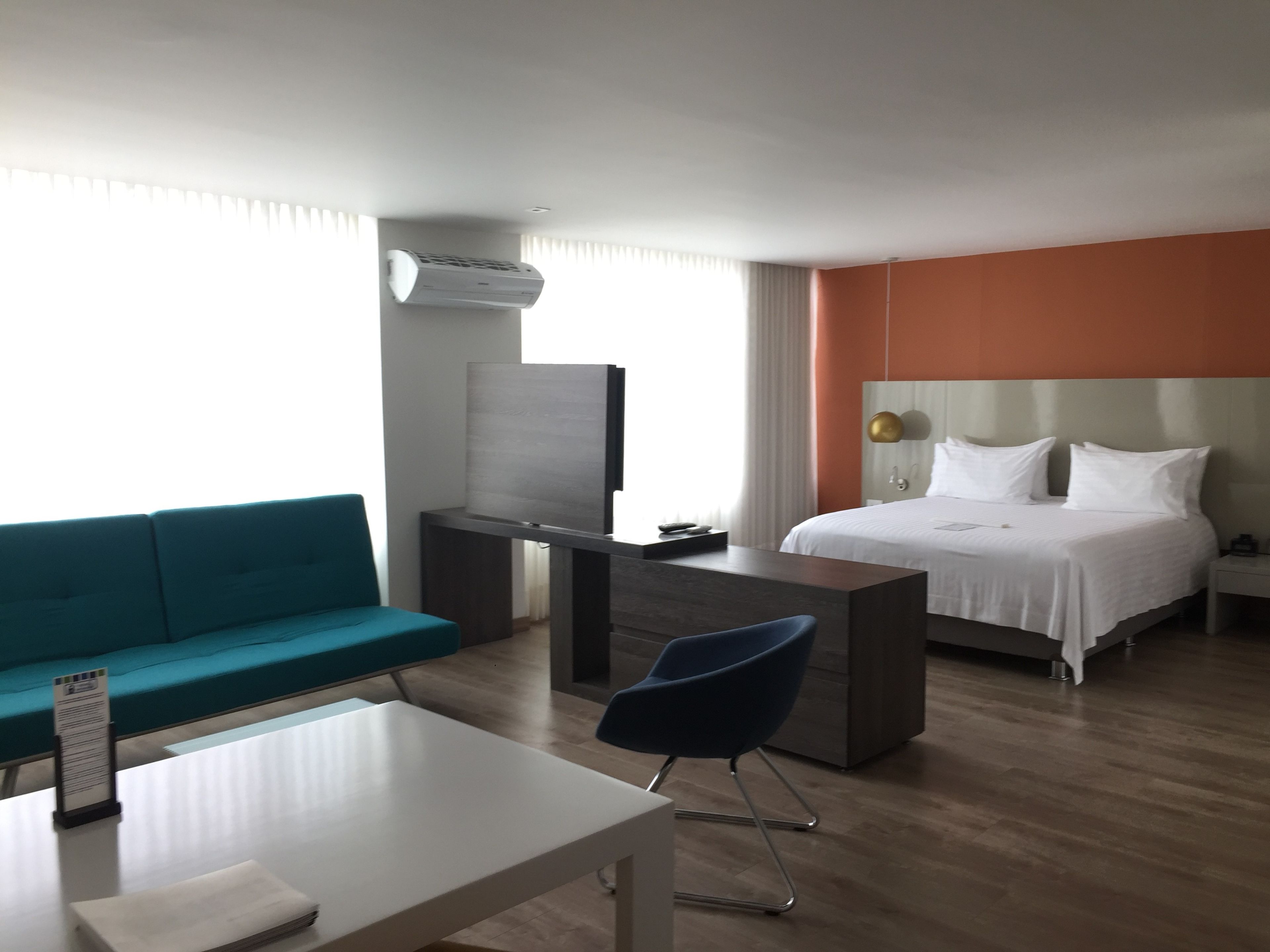 Quarto de hotel com cama, televisão, escrivaninha, cadeira e sofá.