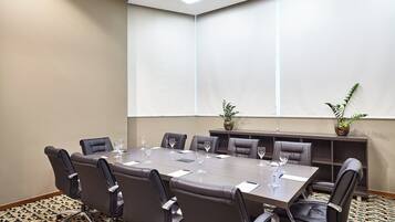 Uma sala de conferências com uma mesa grande, cadeiras de couro e uma tela de projetor.