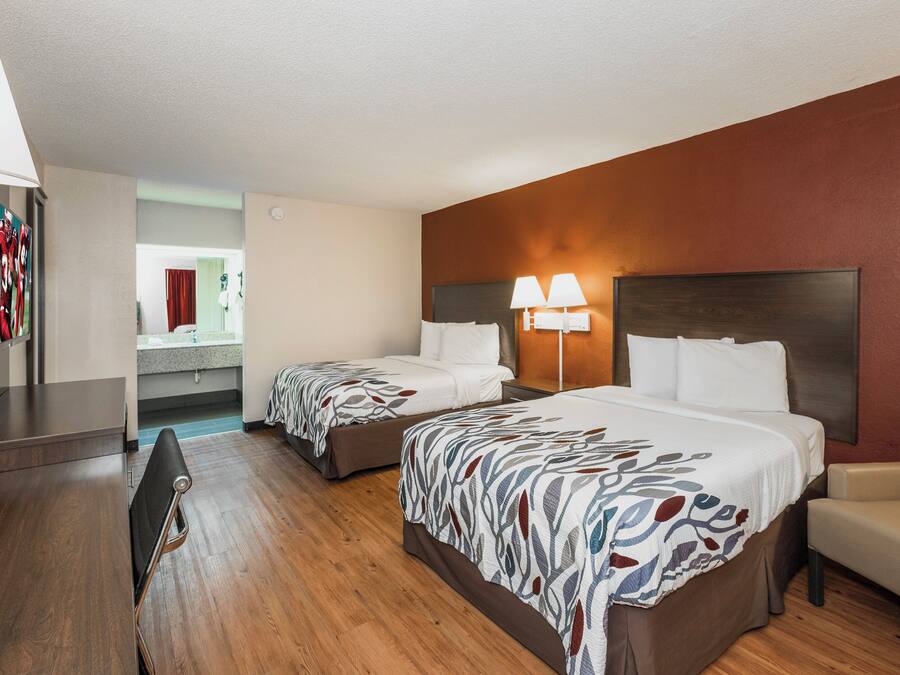 Quarto de hotel com duas camas, uma mesa, uma cadeira e uma televisão.