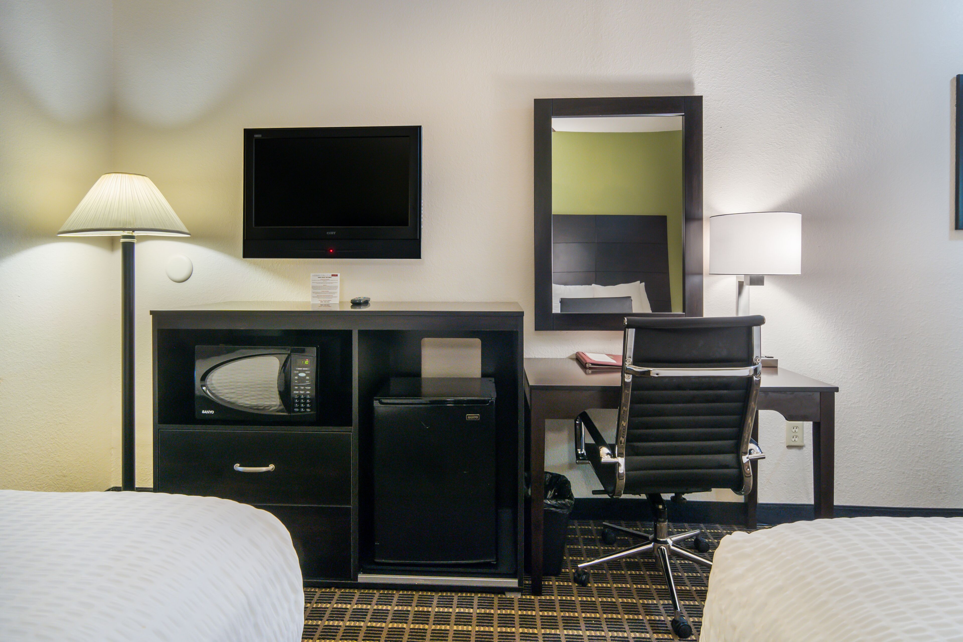 Quarto de hotel com duas camas, uma escrivaninha com cadeira, televisão, micro-ondas, frigorífico e espelho.