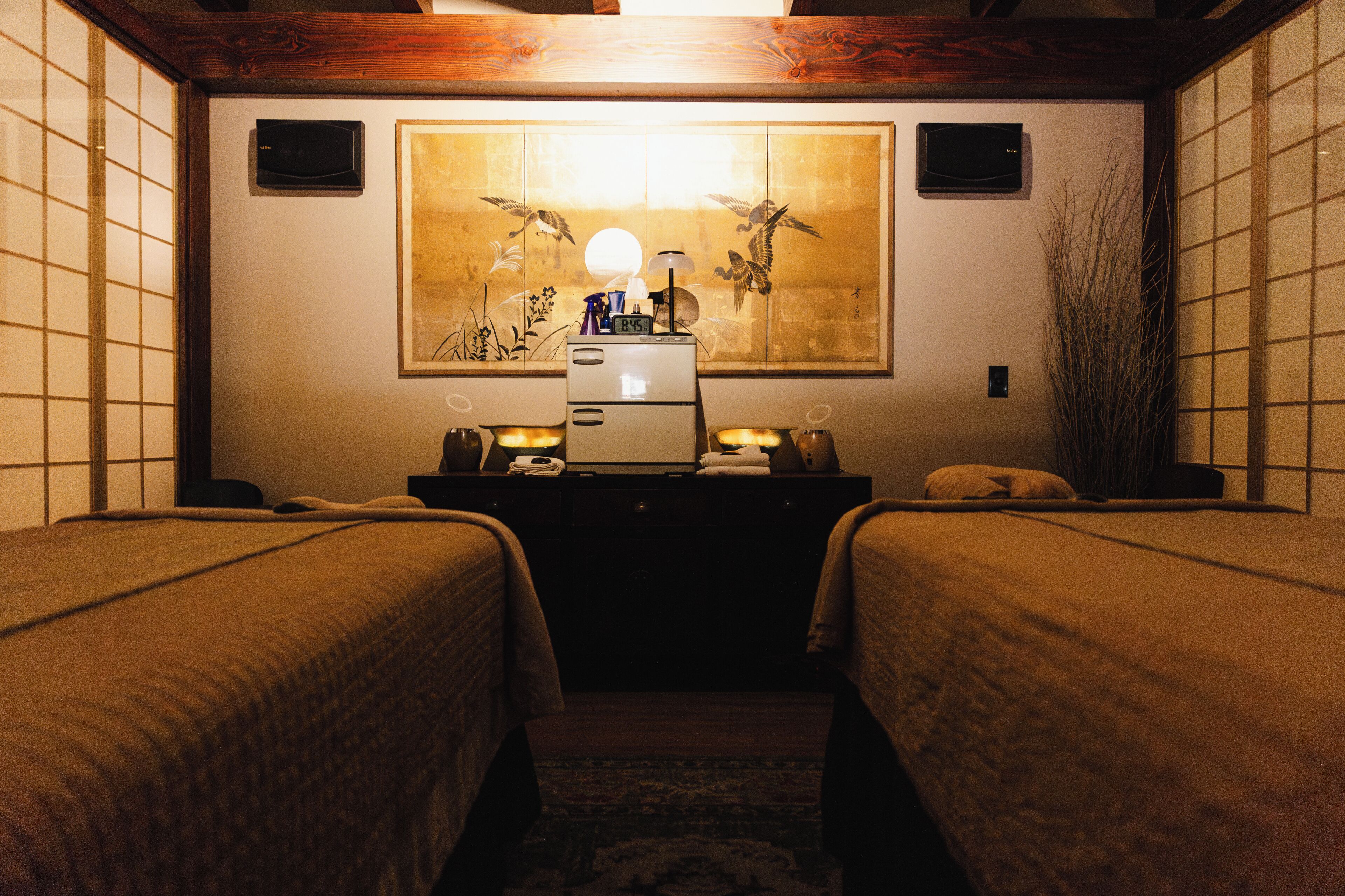 Quarto com duas camas, uma escrivaninha com abajur, um relógio e um quadro na parede.