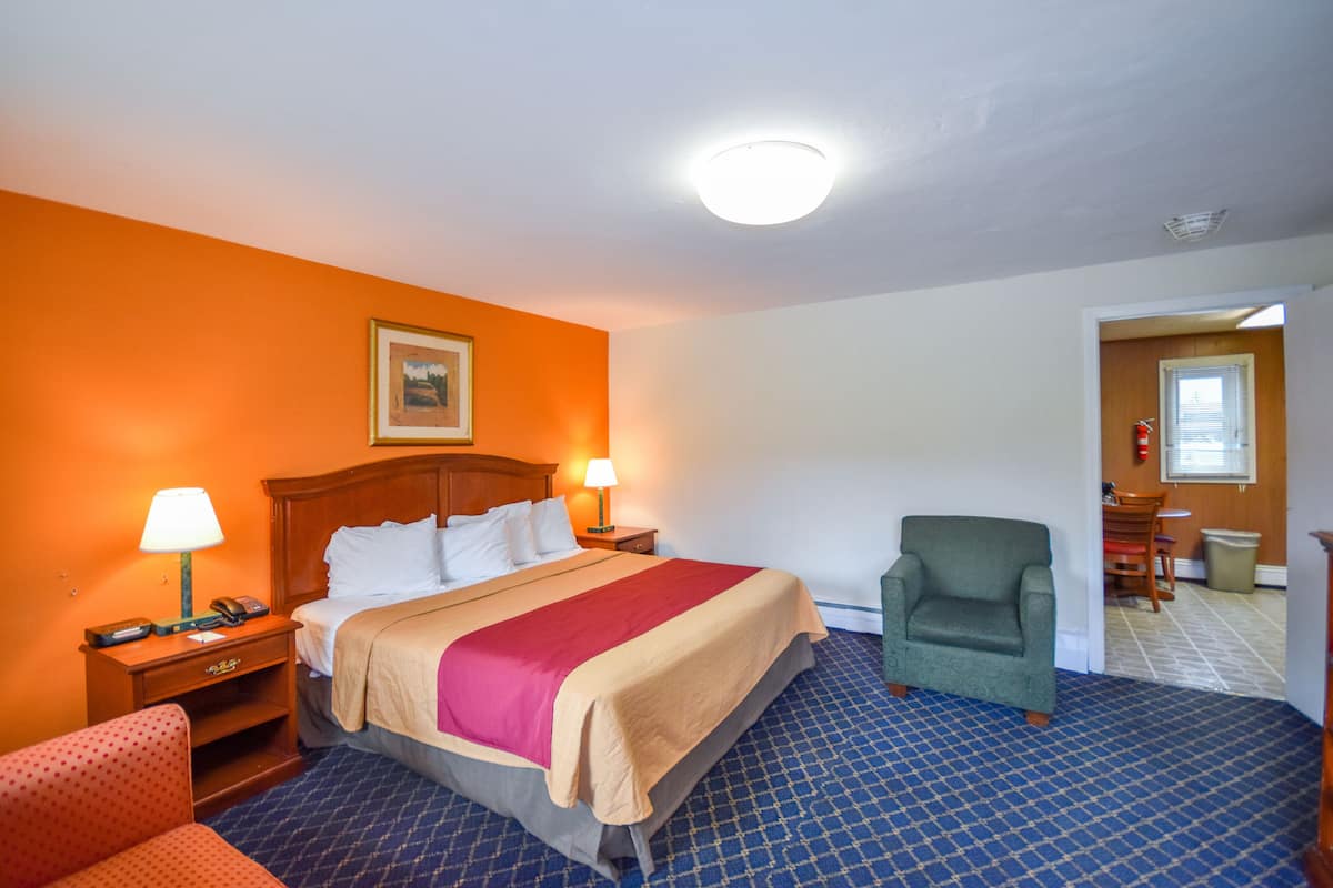 Quarto de hotel com cama, duas luminárias de cabeceira, uma cadeira e um quadro na parede.