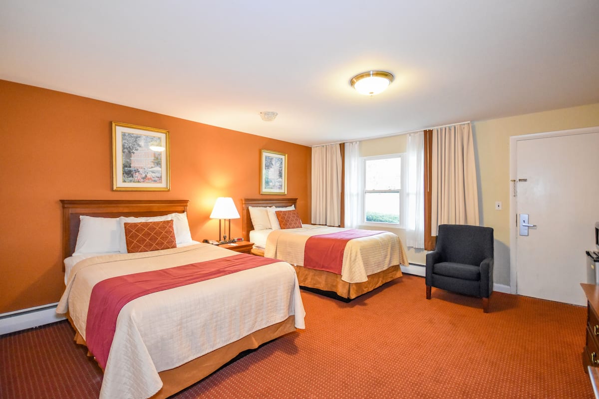 Quarto de hotel com duas camas, uma cadeira e janela com cortinas.