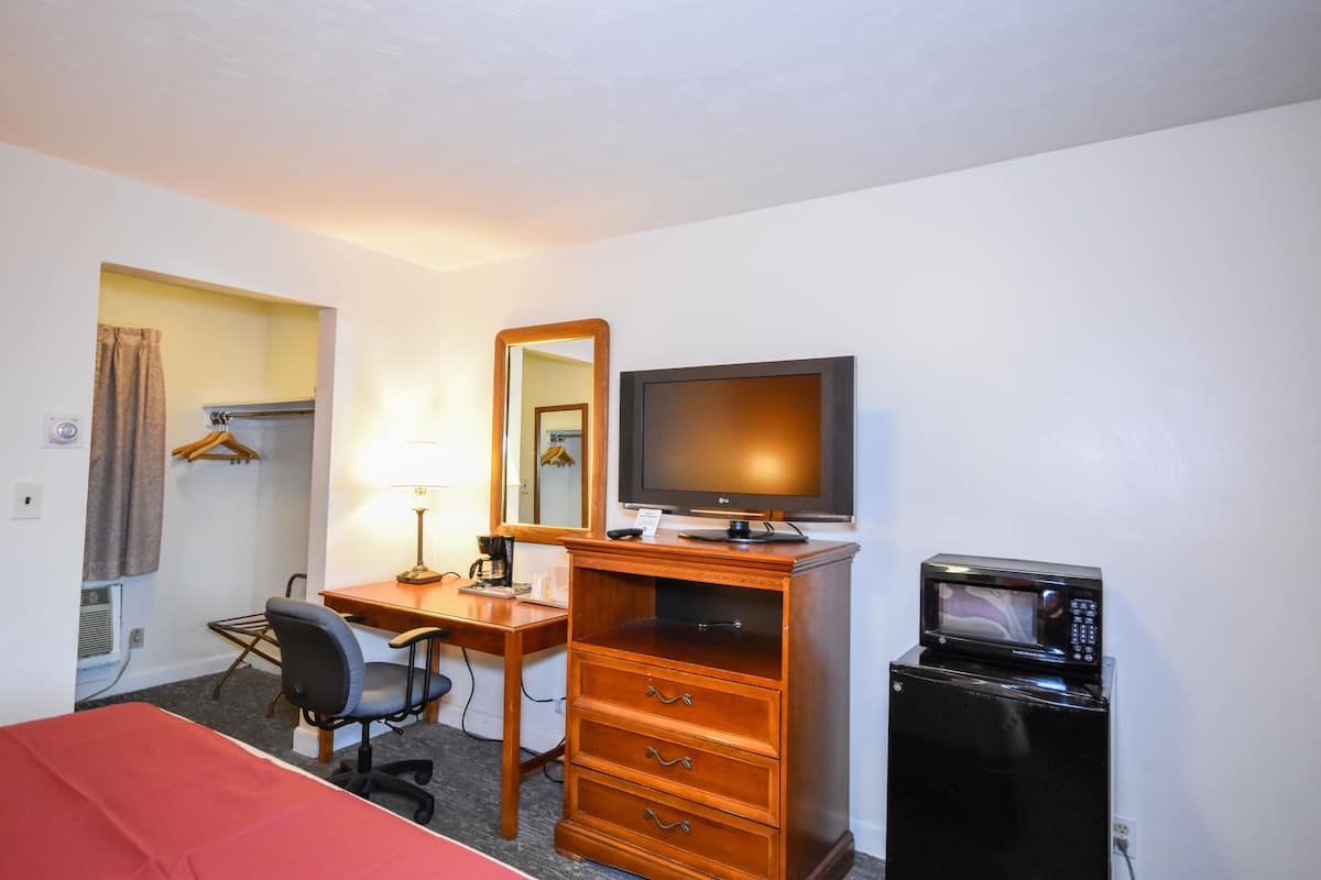 Quarto de hotel com cama, escrivaninha, cadeira, cômoda, televisão e micro-ondas.