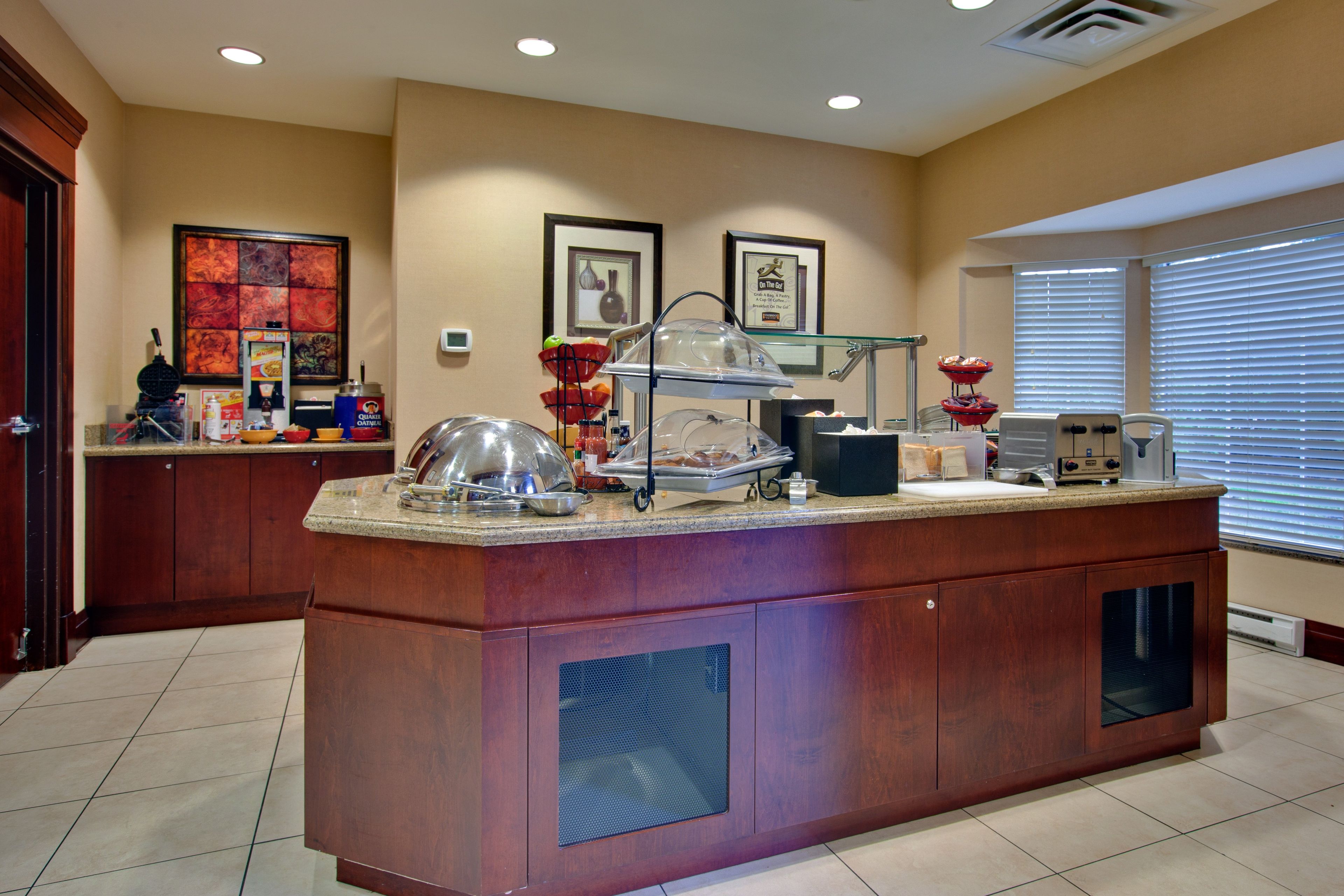 Área de buffet com variedade de alimentos, um espaço para café e uma janela com persianas.