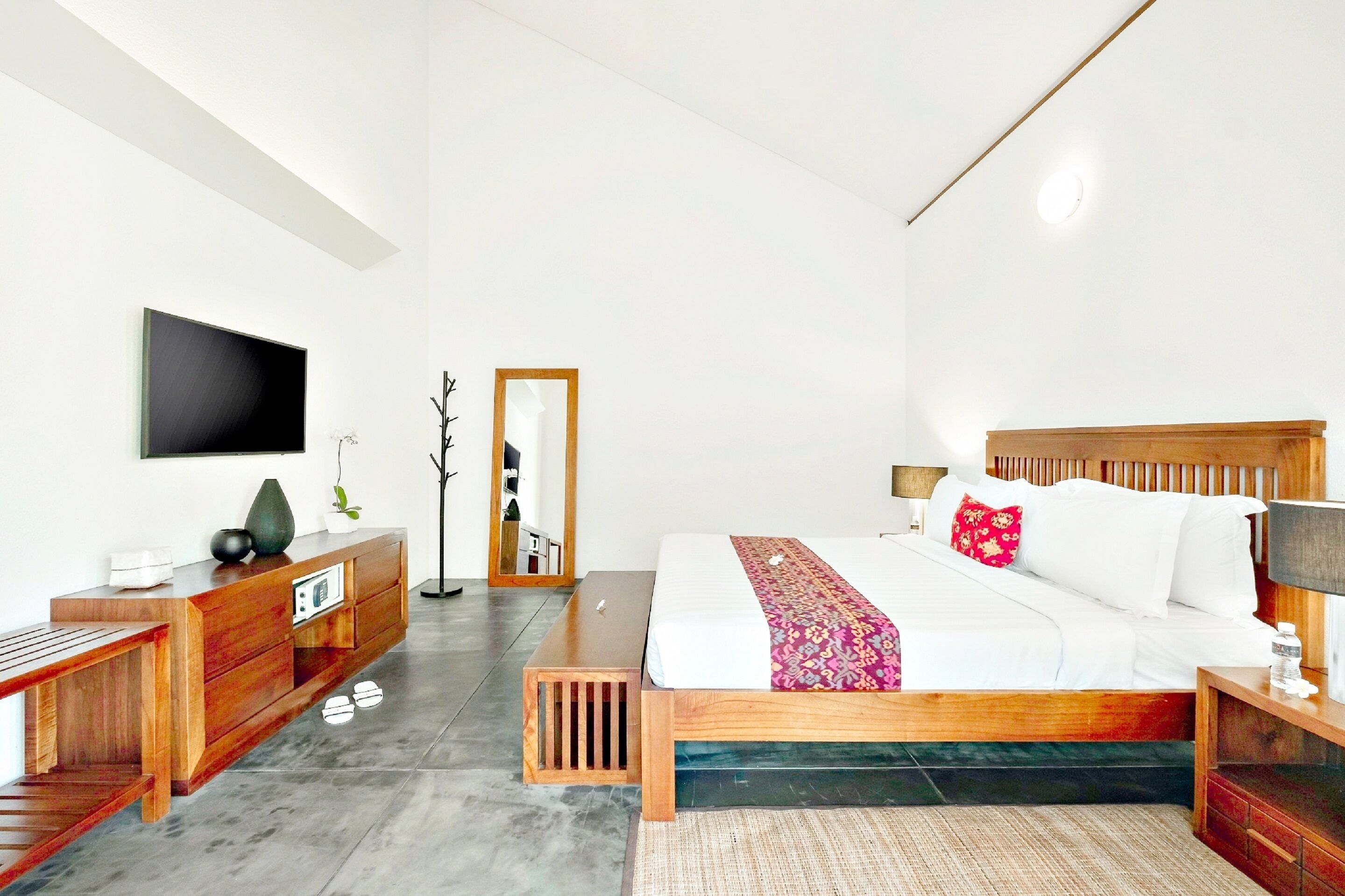 Quarto de hotel moderno com cama de madeira, televisão de tela plana na parede, mesa de cabeceira de madeira e pequena escrivaninha com luminária.