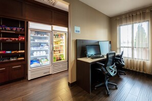 Quarto de hotel com escrivaninha, duas cadeiras, geladeira abastecida com bebidas e um aviso de 'Não Comer ou Beber'.