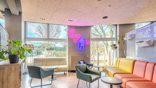 Uma área de estar moderna com assentos, um letreiro de neon e grandes janelas.