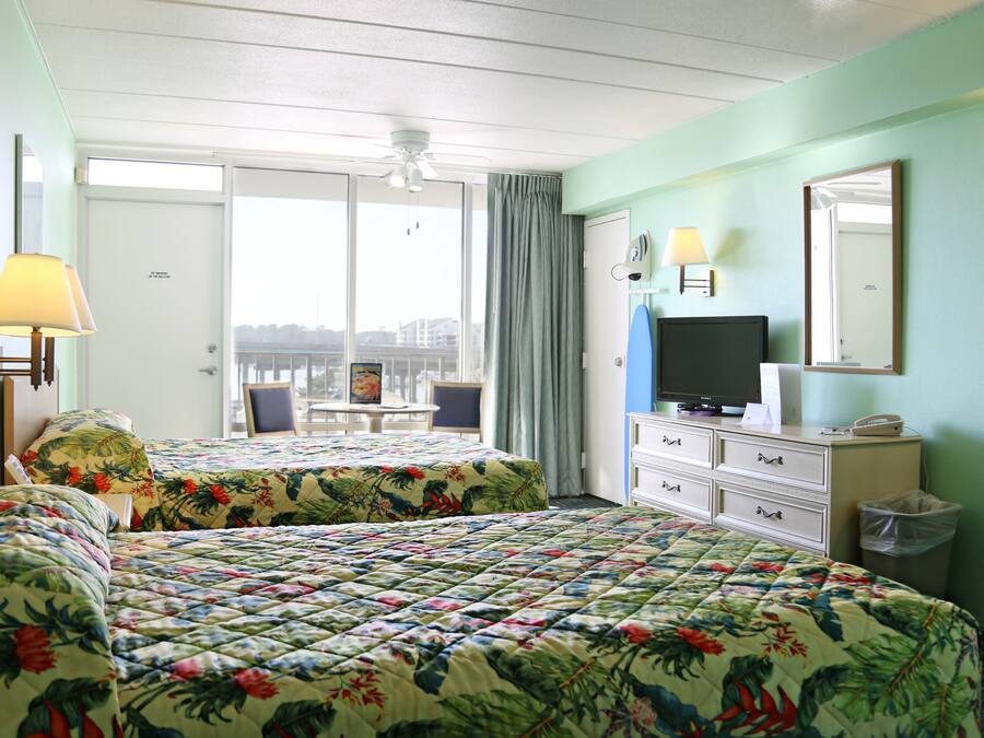 Quarto de hotel com duas camas, televisão, cômoda e janela com vista para edifícios.