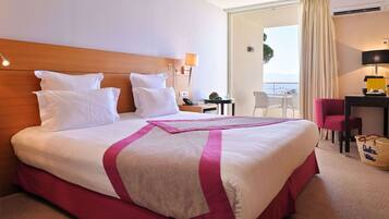 Quarto de hotel com uma cama grande, uma escrivaninha com cadeira, uma mesinha e vista para o exterior.