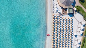 Vista aérea de um resort à beira-mar, com área de piscina, espreguiçadeiras e guarda-sóis.