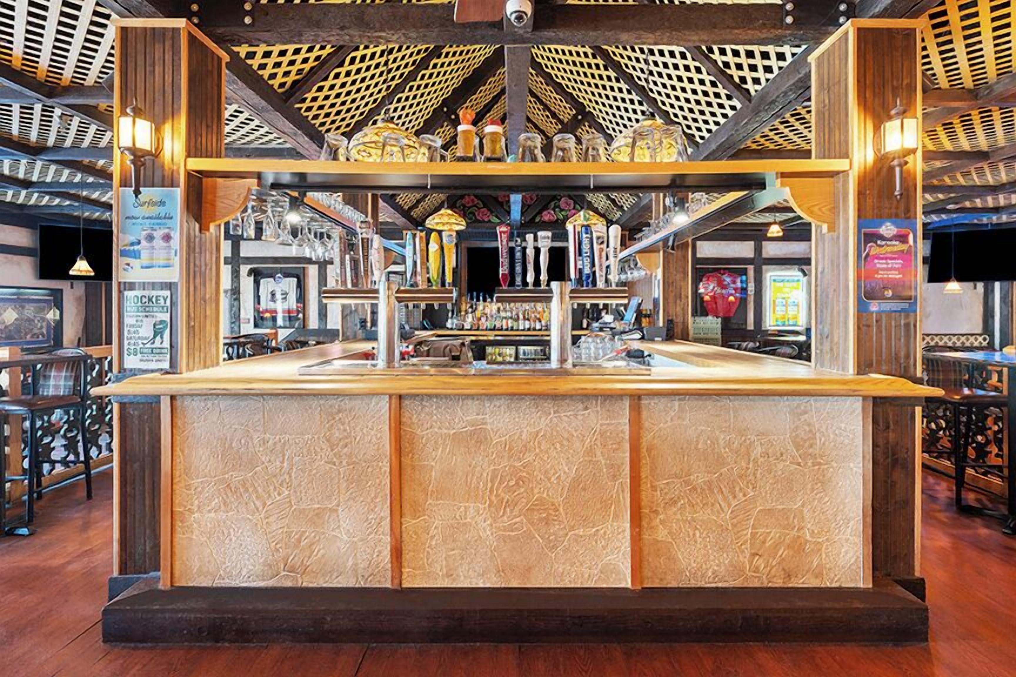 Uma área de bar com um balcão central, prateleiras com garrafas e estrutura de teto em madeira.