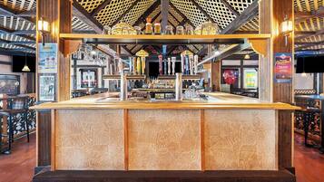 Uma área de bar com um balcão central, prateleiras com garrafas e estrutura de teto em madeira.