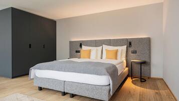 Um quarto moderno com uma cama grande, cabeceira cinza e uma pequena mesa de cabeceira.