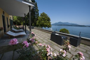 Um terraço com mesas ao ar livre, vista para o lago e montanhas ao fundo.