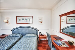 Quarto de hotel com uma cama, uma escrivaninha, uma cadeira, uma mesinha de cabeceira e um espelho.