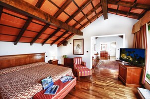 Um quarto espaçoso com uma cama grande, teto de madeira, televisão e uma poltrona de braço listrada de vermelho.