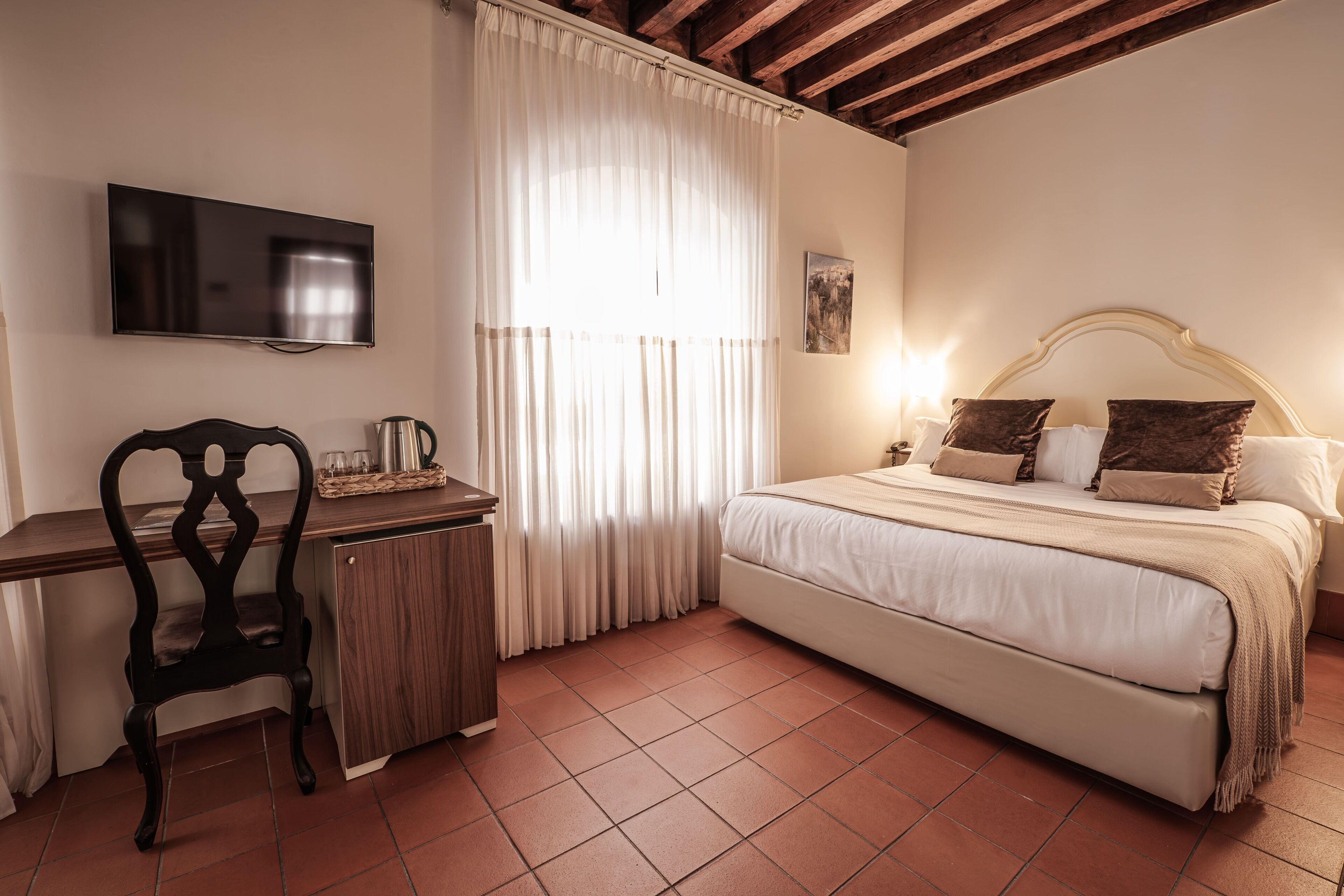 Quarto com uma cama, uma escrivaninha com cadeira, televisão e janela com cortinas.
