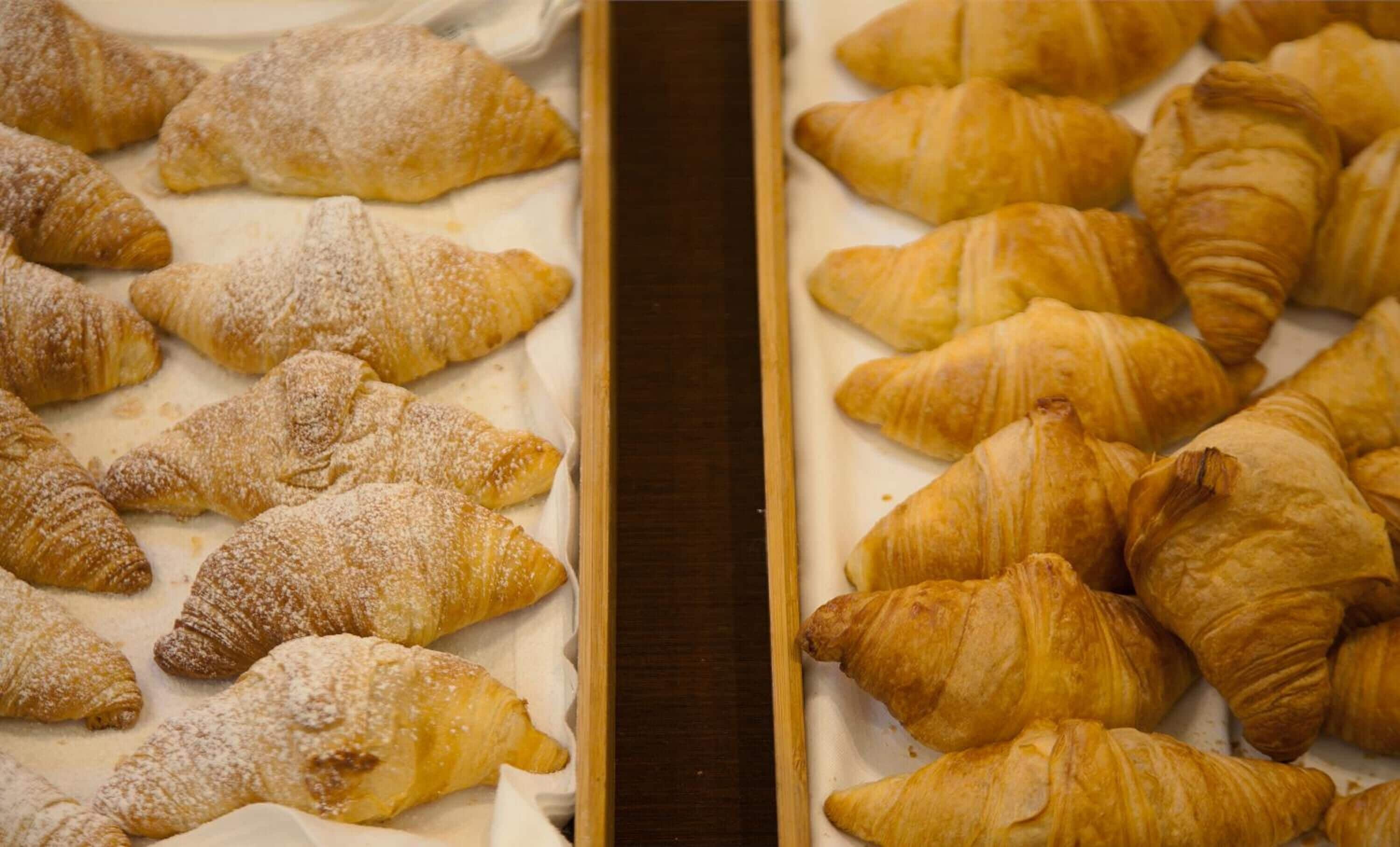 Uma variedade de pastelaria, incluindo croissants e outros produtos de panificação, dispostos em bandejas.