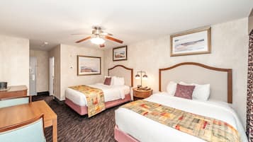 Quarto de hotel com duas camas, uma escrivaninha, uma cadeira, ventoinha no teto e obras de arte nas paredes.