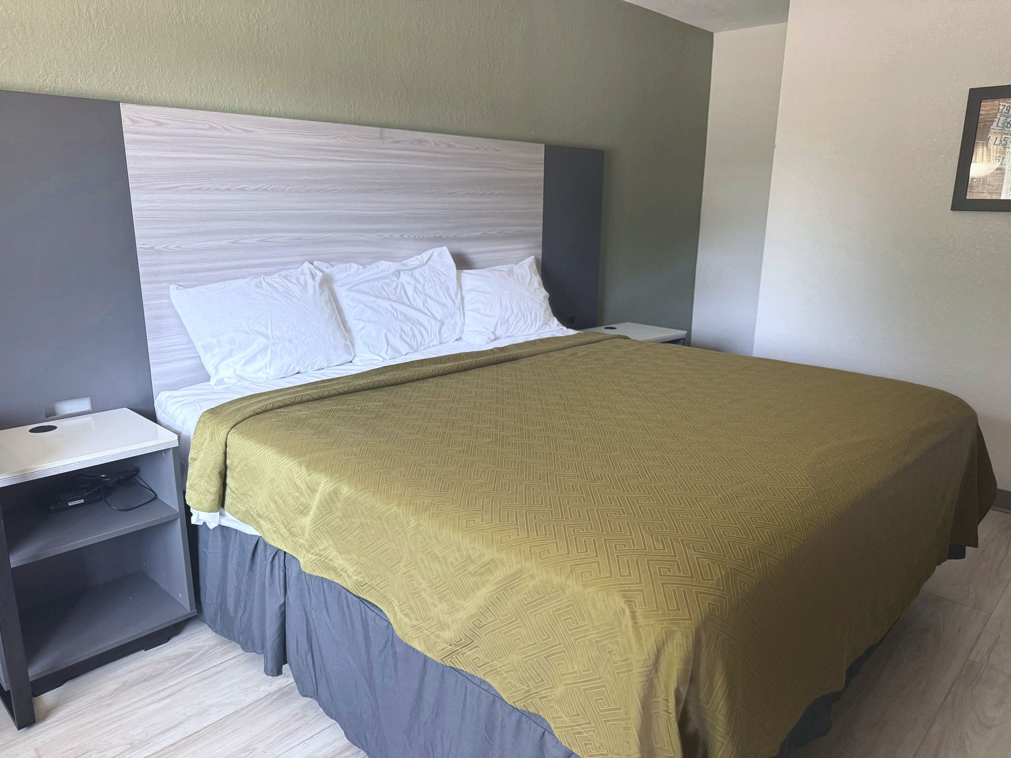 Quarto de hotel com cama, mesa de cabeceira e criado-mudo.