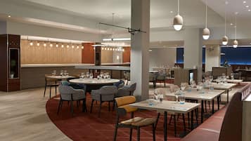 Um restaurante moderno com mesas redondas, cadeiras e luminárias pendentes.