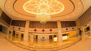 Um hall amplo com um design circular imponente no teto, um lustre central e um balcão de recepção.