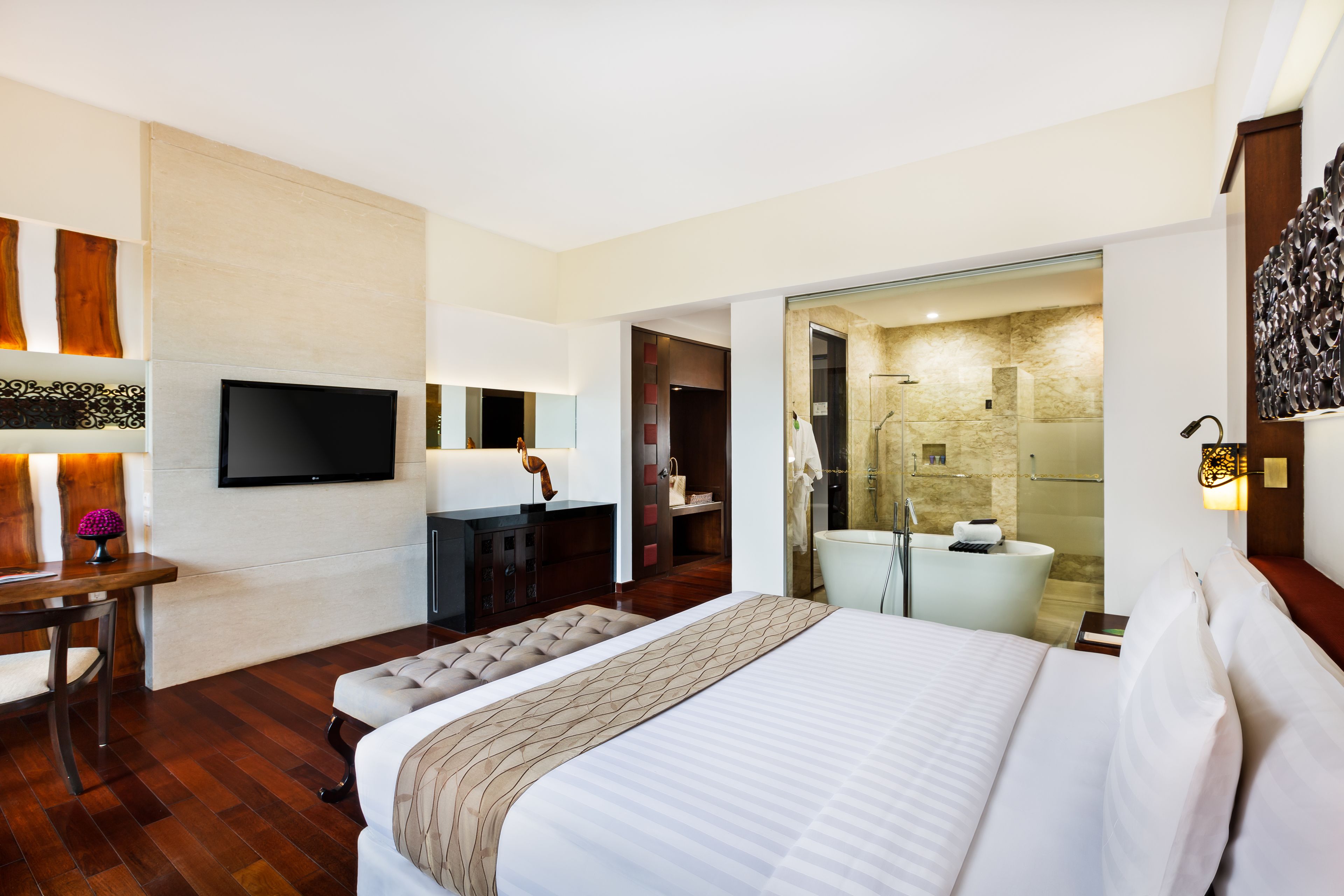 Quarto de hotel moderno com uma cama grande, televisão de tela plana, escrivaninha e banheiro com chuveiro de vidro.