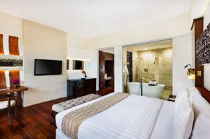 Quarto de hotel moderno com uma cama grande, televisão de tela plana, escrivaninha e banheiro com chuveiro de vidro.