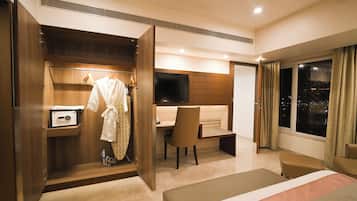 Quarto de hotel com closet espaçoso, escrivaninha, cadeira, cama e televisão.