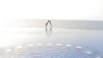 Um casal está em pé na praia, com um mar calmo ao fundo.