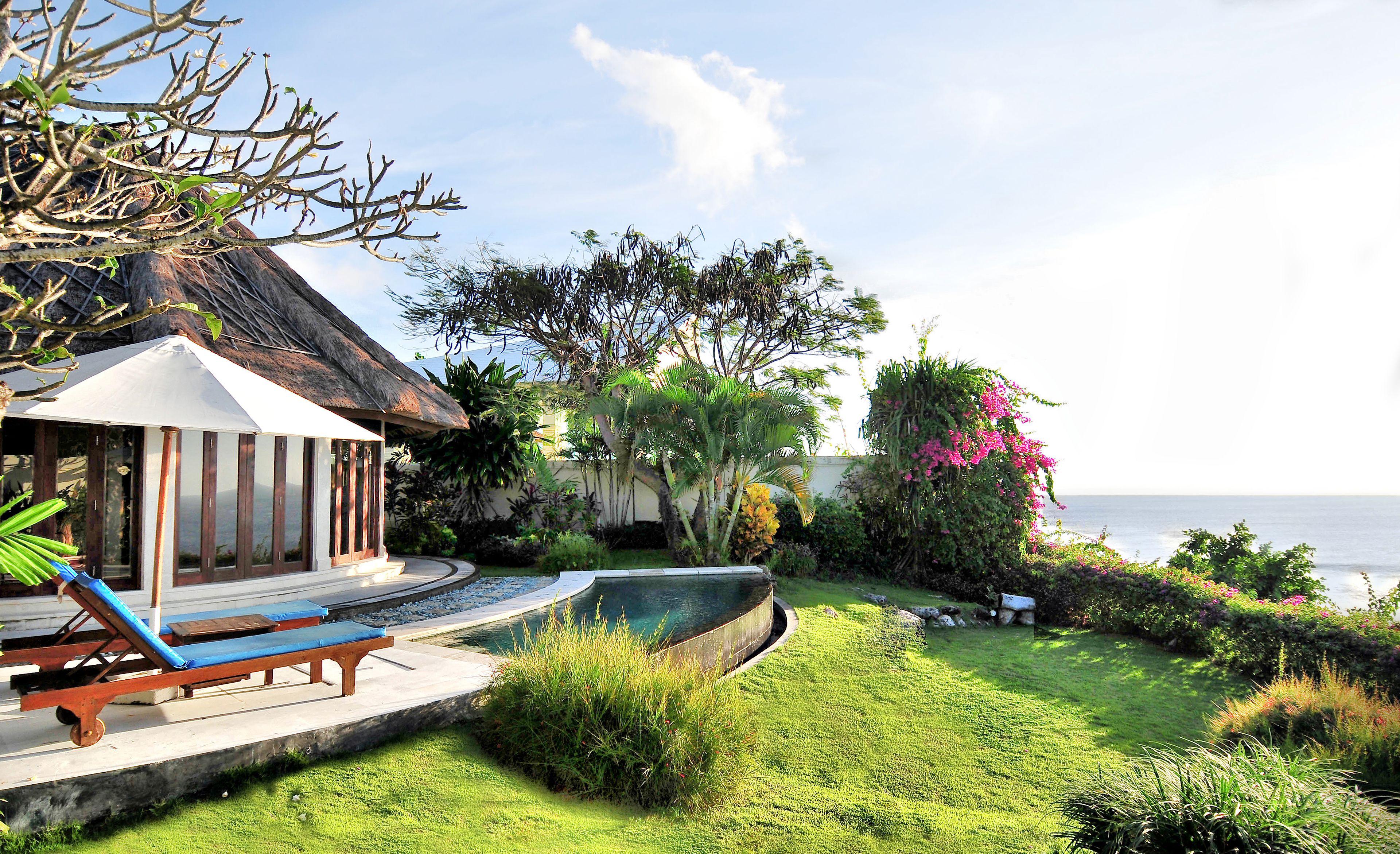 Um resort tropical com uma cabana de telhado de palha, piscina e vegetação exuberante.