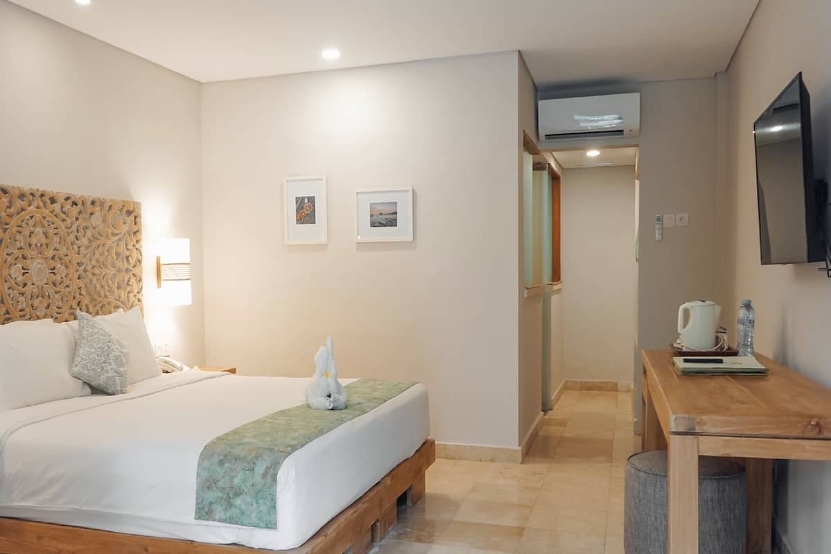 Quarto de hotel com cama, cabeceira de madeira, escrivaninha com cadeira, televisão e quadros nas paredes.