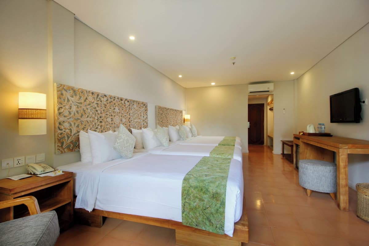 Quarto de hotel com uma cama grande, mesas de cabeceira, escrivaninha, televisão e ar condicionado fixado na parede.