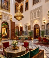 Interior luxuoso com arcos ornamentados, um lustre imponente e uma área de estar com mesa de mármore.