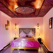 Quarto com cama, duas mesas de cabeceira e teto estampado.