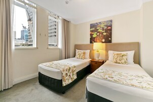 Quarto de hotel com duas camas, uma janela com cortinas, um quadro na parede e um abajur na mesa de cabeceira.