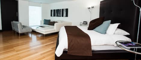 Quarto de hotel moderno com uma cama grande, um sofá, uma poltrona e uma escrivaninha.