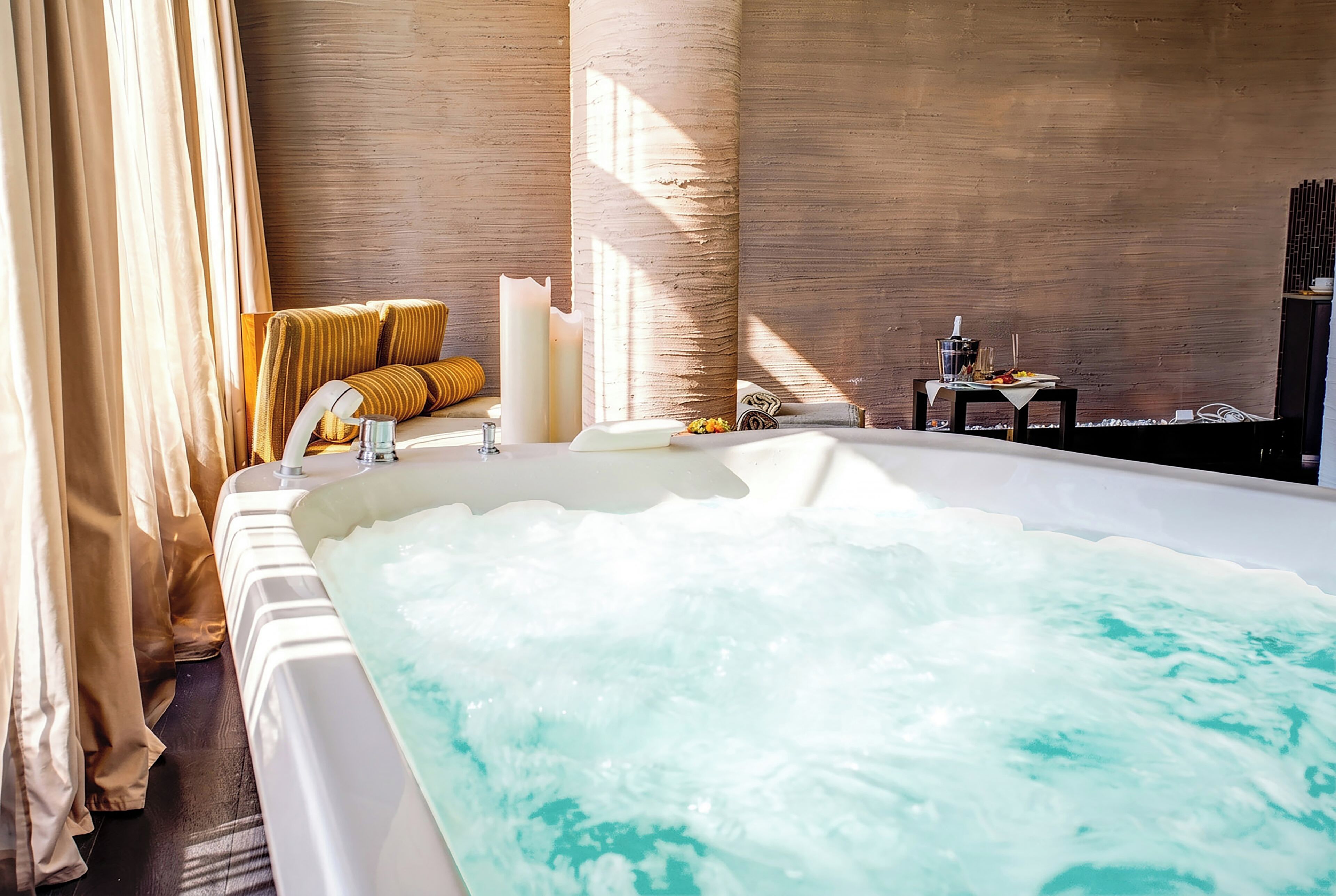 Um quarto de spa com uma banheira grande, uma parede de madeira e uma pequena mesa com uma garrafa e copos.