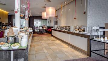 Uma ampla área de buffet com diversas estações de serviço e luzes decorativas pendentes.