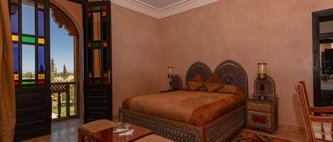 Quarto com uma cama grande, uma cadeira de madeira, uma mesinha e uma mesa de cabeceira com luminárias.