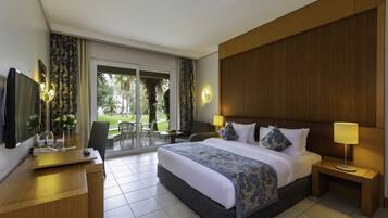 Quarto de hotel com uma cama grande, uma escrivaninha com computador, uma televisão e vista para o exterior.