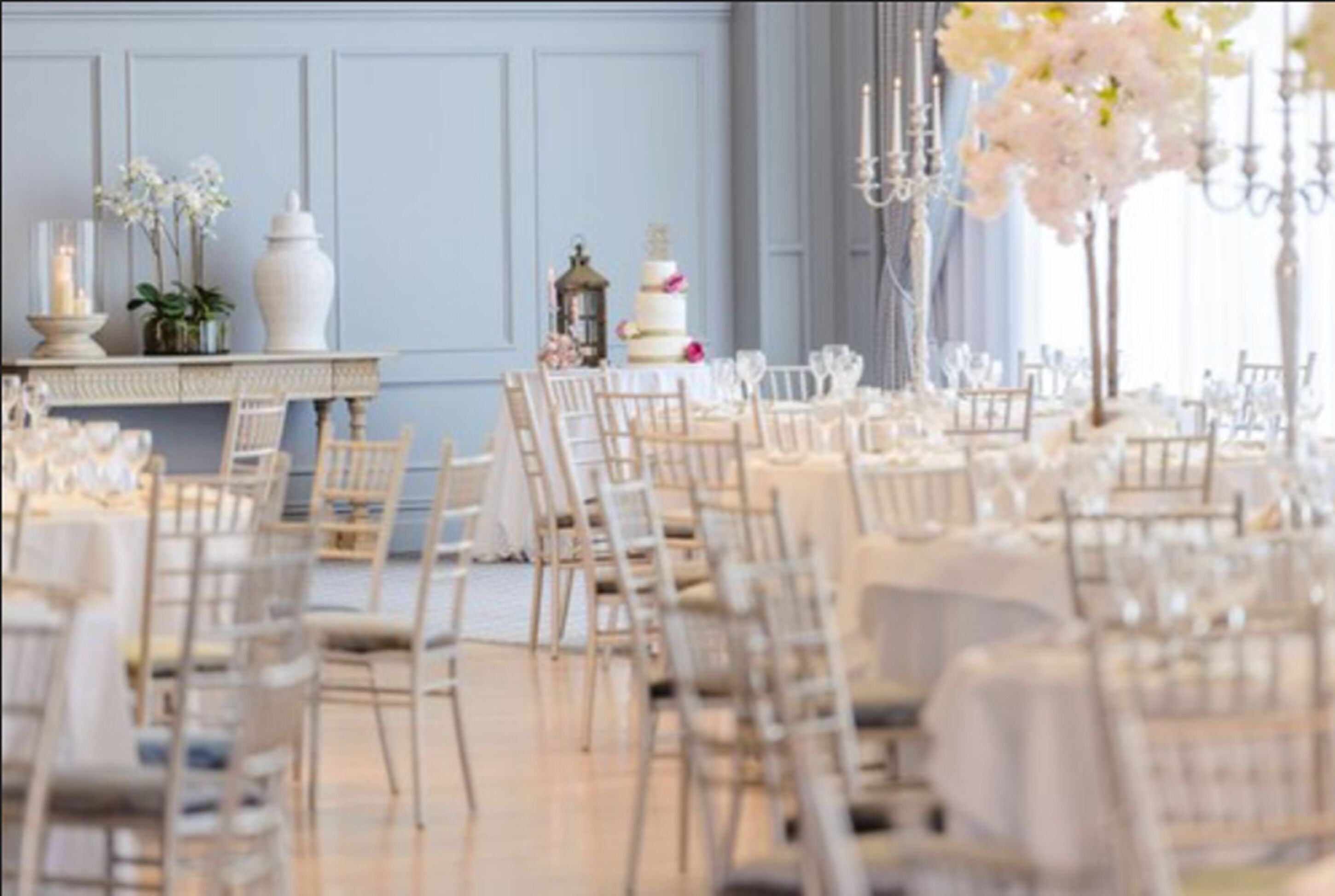 Uma sala de jantar formal com mesas redondas, cadeiras brancas e um candelabro.