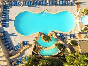 Vista aérea de uma área de piscina em resort, com vários espreguiçadeiras e uma piscina central.