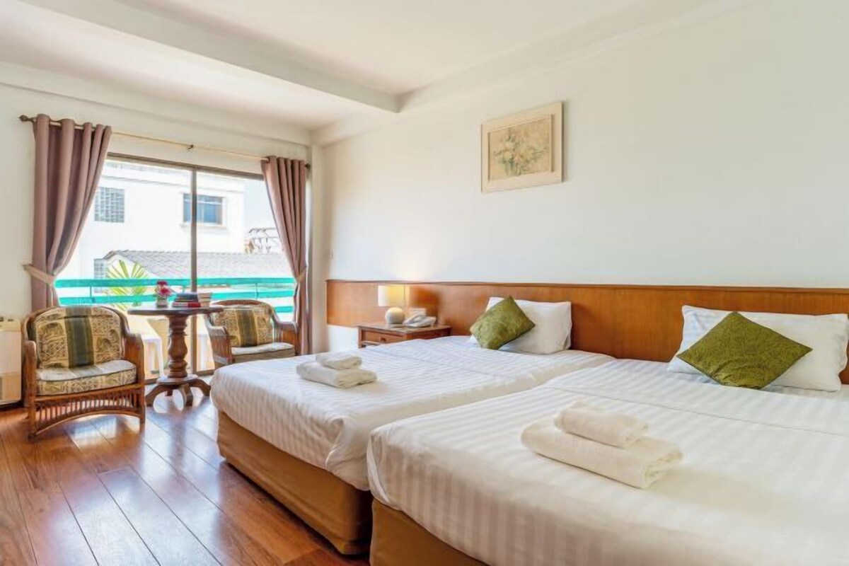 Quarto de hotel com duas camas, uma mesa com cadeiras, vista para o mar e um quadro na parede.