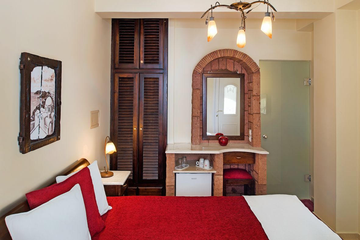 Quarto de hotel com cama, escrivaninha, pequeno espaço de cozinha e banheiro com espelho e chuveiro.