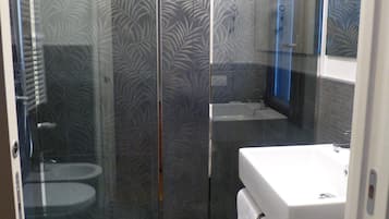 Um banheiro moderno com chuveiro em box de vidro, pia branca e vaso sanitário.