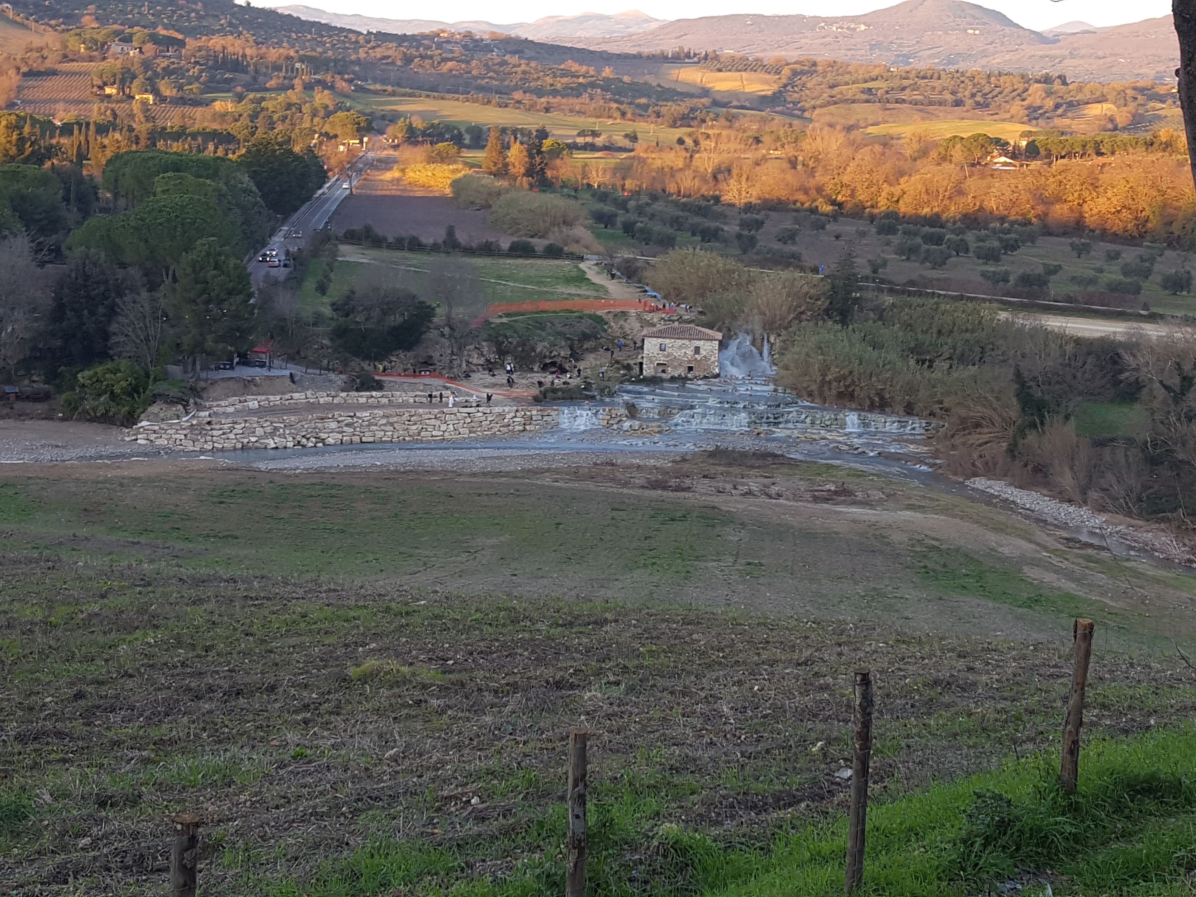 Paisagem rural com uma ponte de pedra, um rio corrente e uma cordilheira ao longe.