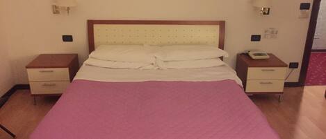 Quarto de hotel padrão com uma cama de solteiro, duas mesas de cabeceira e uma imagem de ovelhas pendurada na parede.